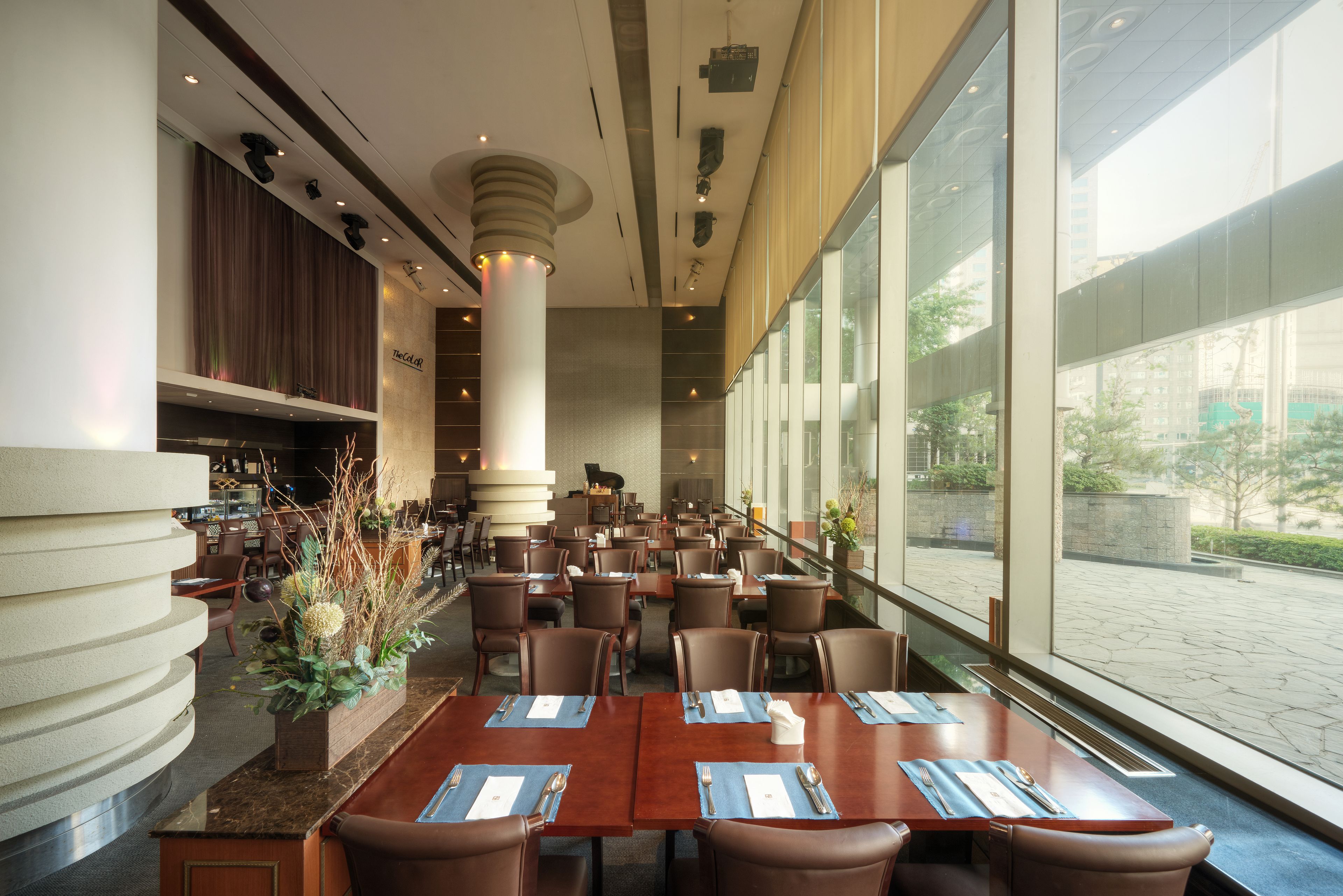 Um restaurante amplo, com pé direito alto, grandes janelas e decoração moderna.