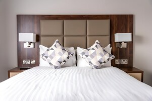 Quarto de hotel com uma cama grande, duas mesas de cabeceira e duas luminárias de parede.
