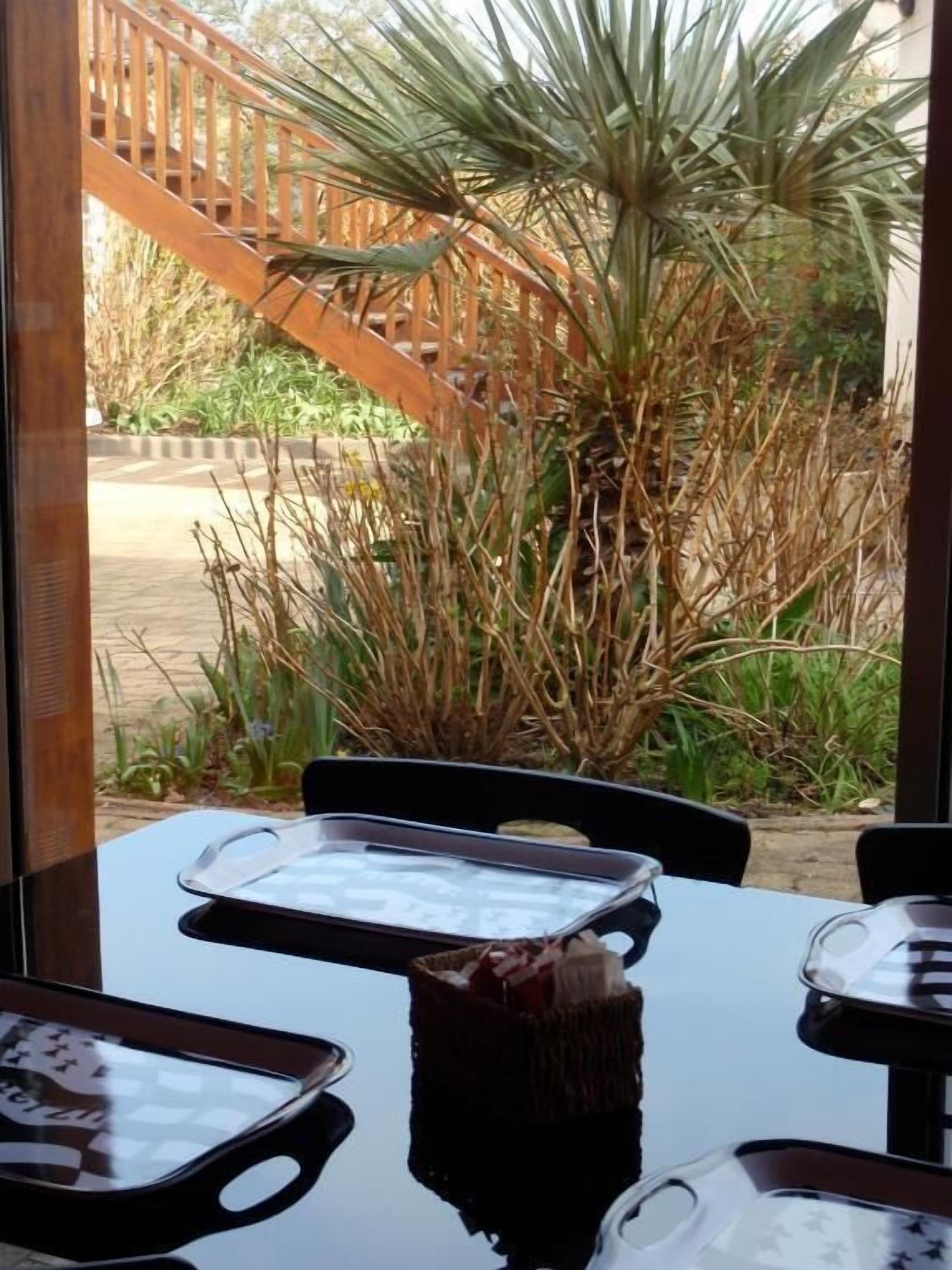 Uma mesa com bandeja e bolo, uma cadeira, e vista para uma escadaria de madeira e plantas.