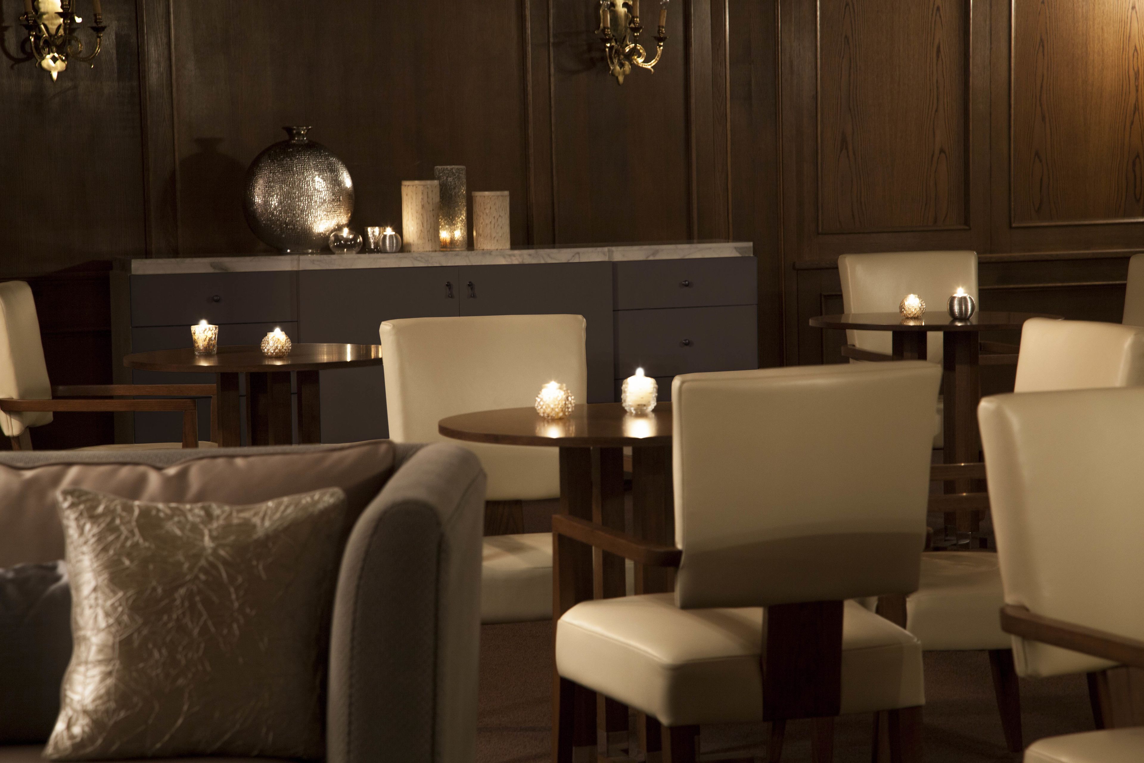 Uma área de estar com pouca luz, com um sofá, cadeiras e uma mesa pequena com velas.