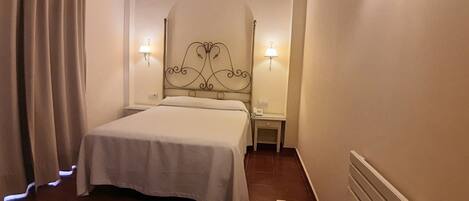 Quarto de hotel com uma cama, duas mesas de cabeceira e duas luminárias fixadas na parede.