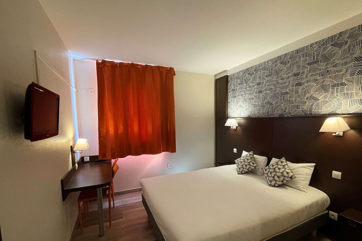 Quarto de hotel com uma cama, uma escrivaninha, uma televisão e parede com padrão.
