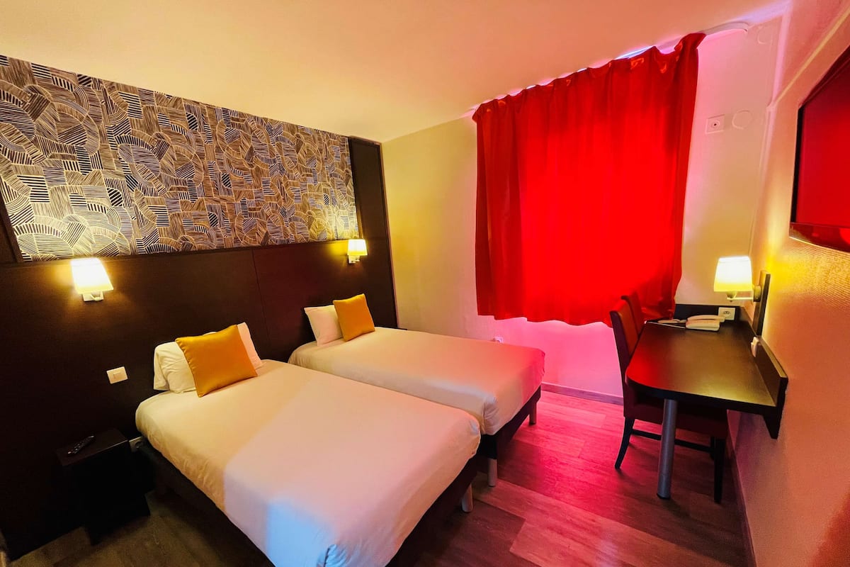 Quarto de hotel com duas camas, uma escrivaninha e uma cadeira.