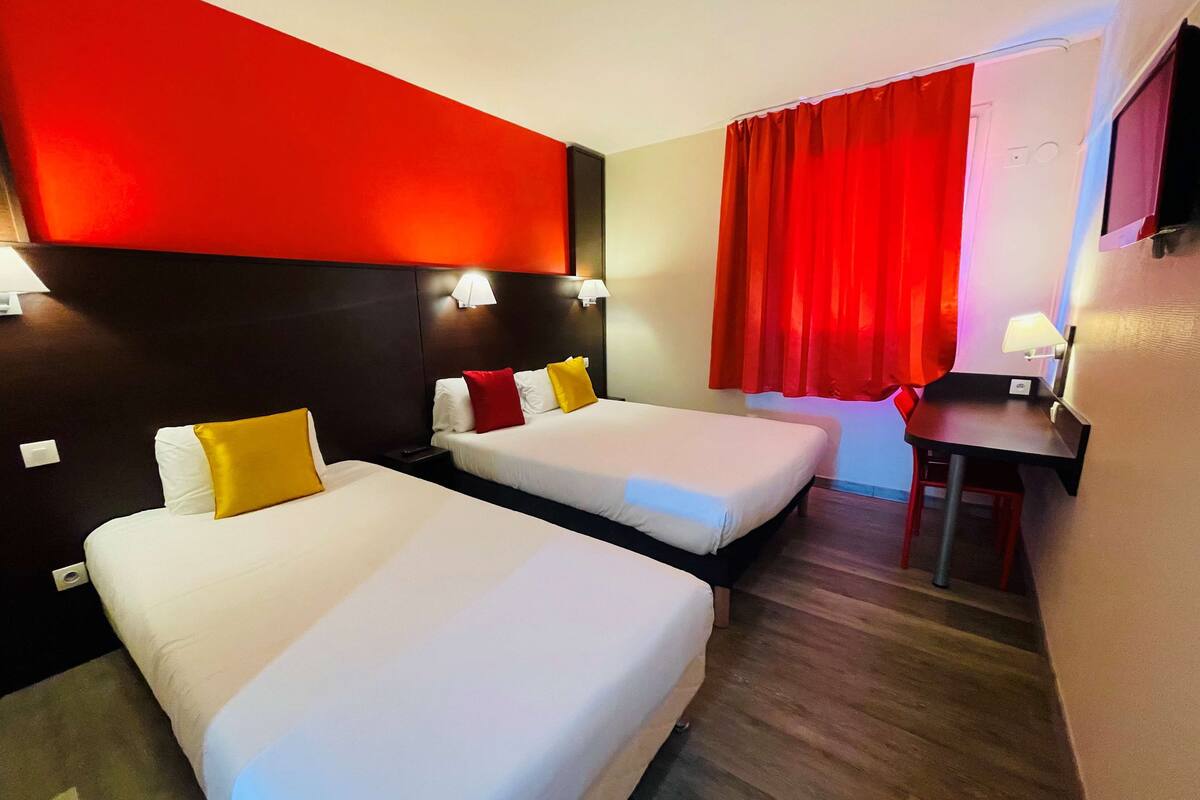 Quarto de hotel com duas camas de solteiro, uma mesa e uma cadeira.
