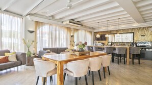 Uma sala de estar ampla com uma mesa de jantar de madeira, assentos confortáveis e uma área de cozinha com bancada.