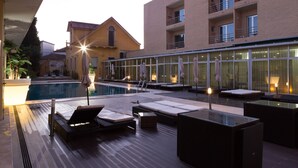 Área de piscina no terraço com espreguiçadeiras e guarda-sóis, uma piscina e um edifício com varandas.