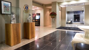 Um lobby moderno com uma mesa de recepção, um quadro na parede, um logotipo na parede e um vaso de plantas com flores vermelhas.