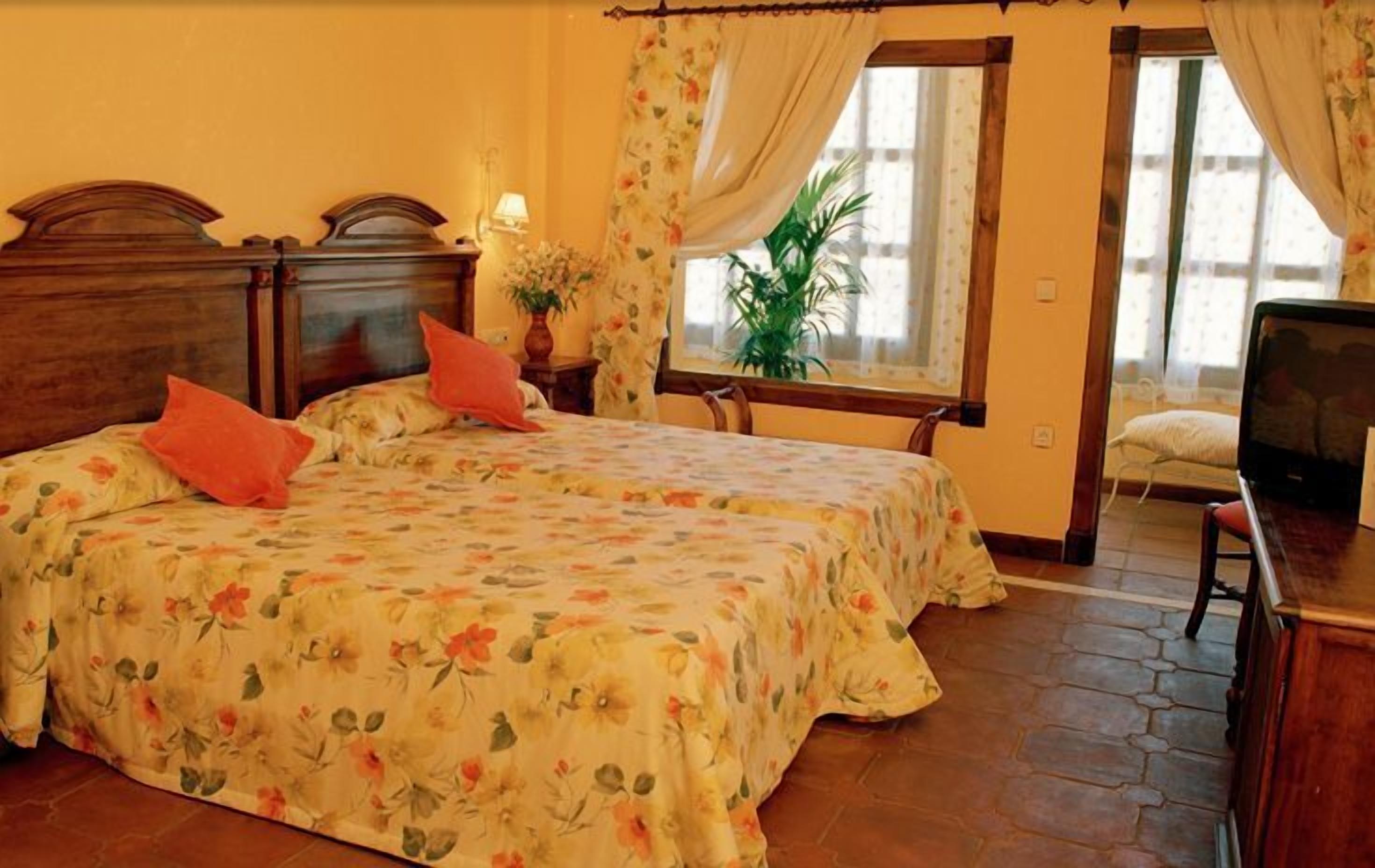 Quarto com duas camas, cabeceira de madeira, mesa de cabeceira, planta em vaso e janela com cortinas.
