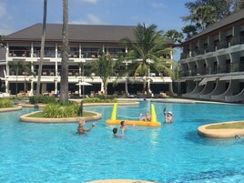 Uma piscina com uma rede, palmeiras e um hotel ao fundo.