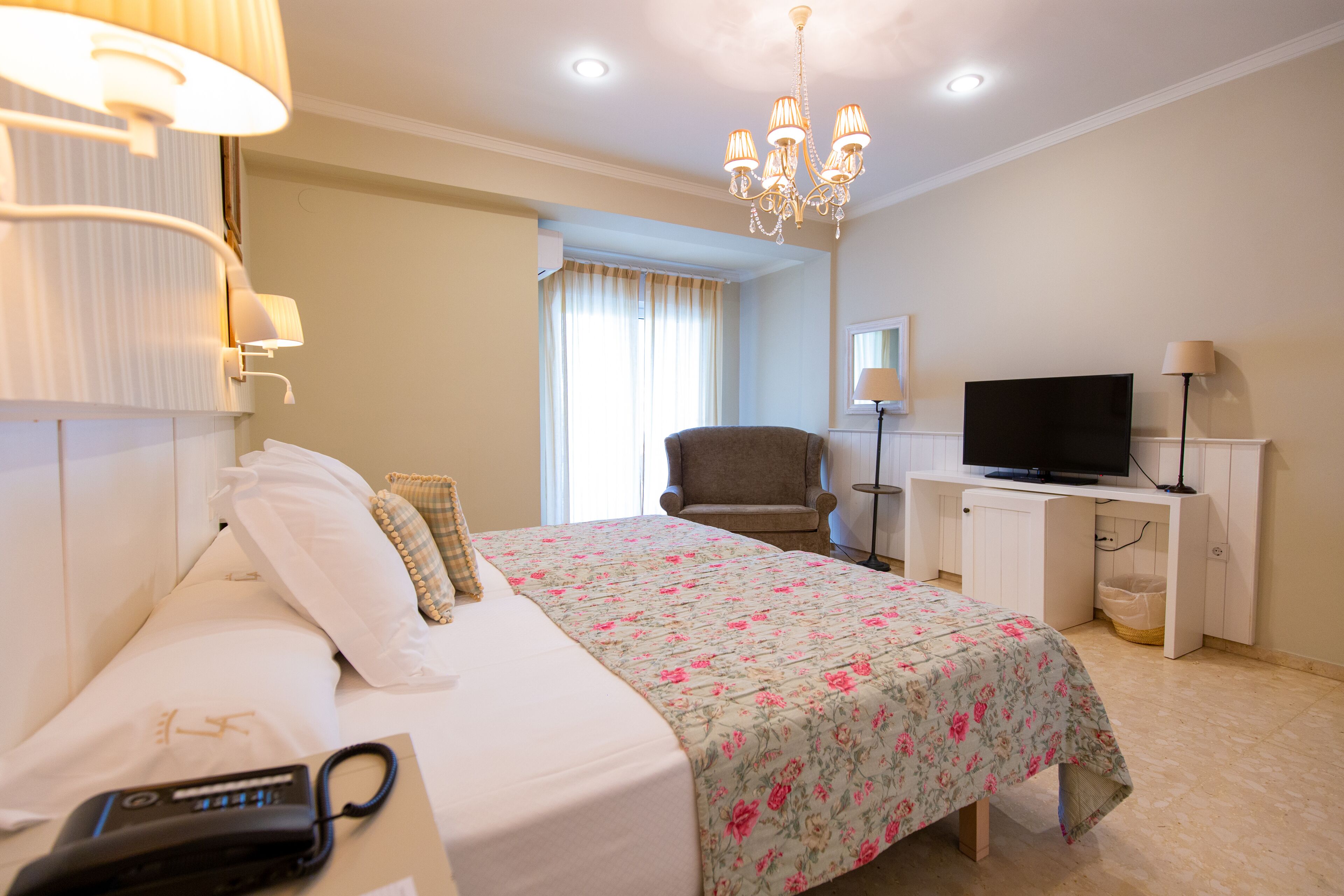 Quarto de hotel com cama, cadeira, televisão e escrivaninha.