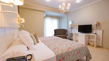 Quarto de hotel com cama, cadeira, televisão e escrivaninha.
