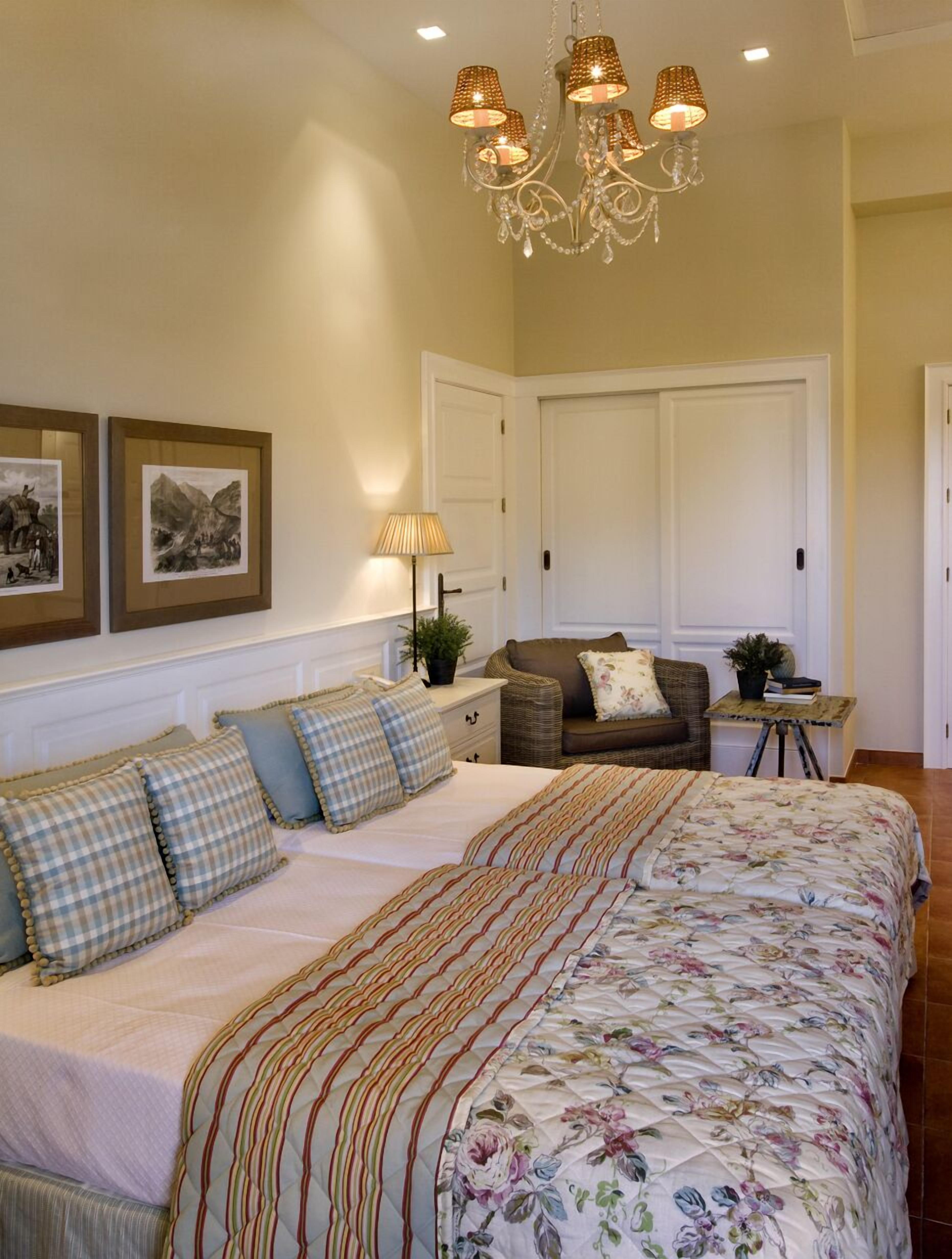 Quarto com uma cama grande, um candelabro, um sofá e quadros nas paredes.