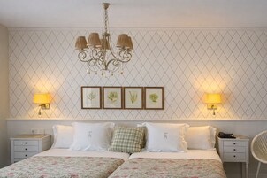 Um quarto com uma cama, duas mesas de cabeceira, uma cadeira, um candelabro e luminárias na parede.