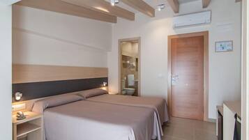 Quarto de hotel moderno com duas camas, teto de madeira, banheiro visível através de uma porta aberta e uma pequena mesa de trabalho com cadeira.