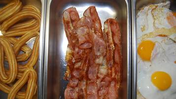 Bandeja de café da manhã com churros, bacon e ovos fritos.