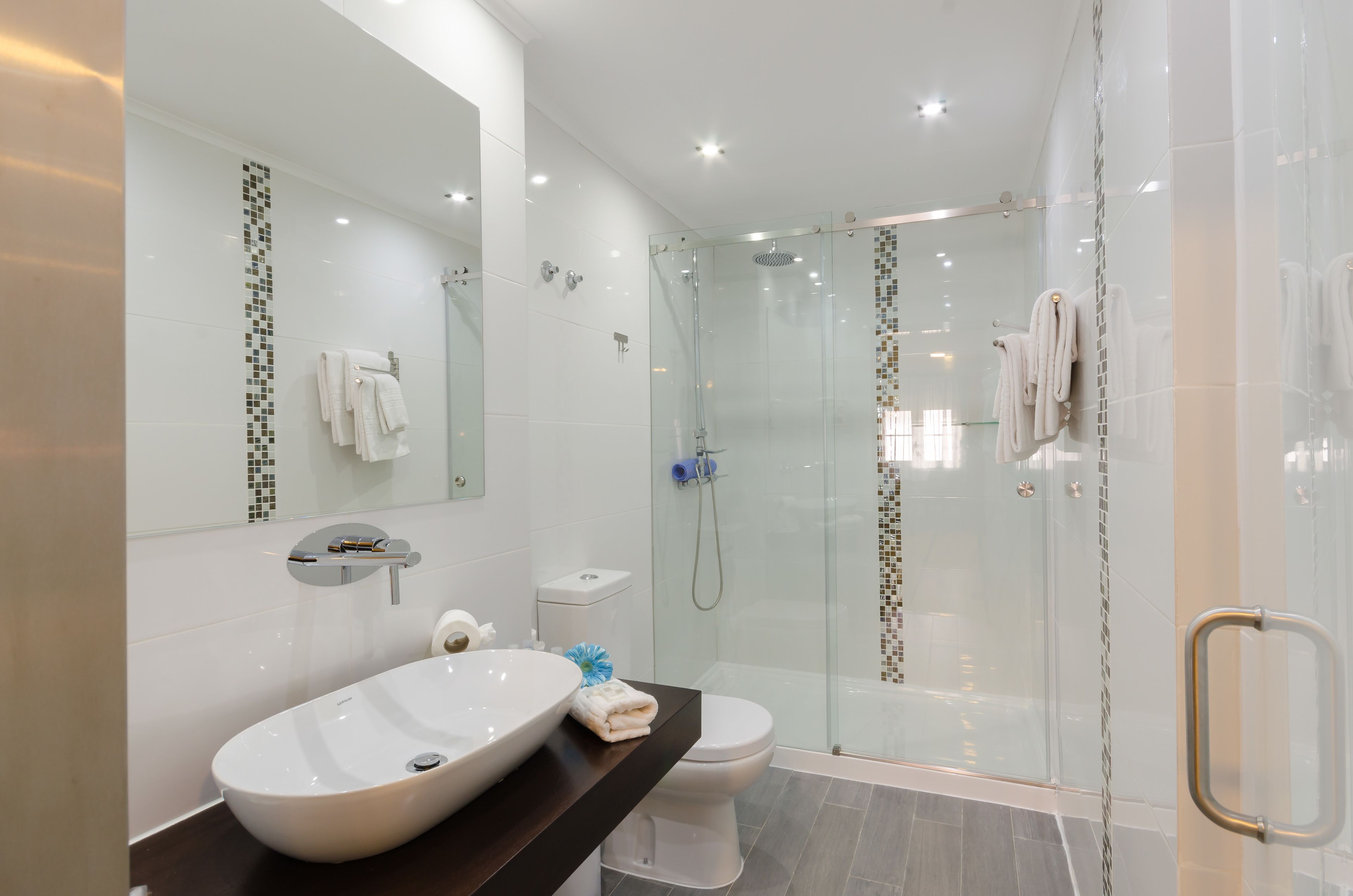 Uma casa de banho moderna com chuveiro em cabine de vidro, lavatório branco e sanita.