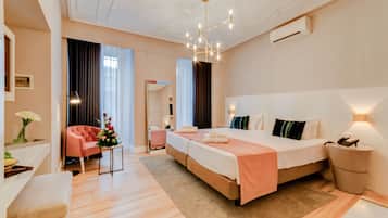 Quarto de hotel moderno com uma cama grande, área de estar com uma poltrona rosa, uma pequena mesa com flores e um abajur.