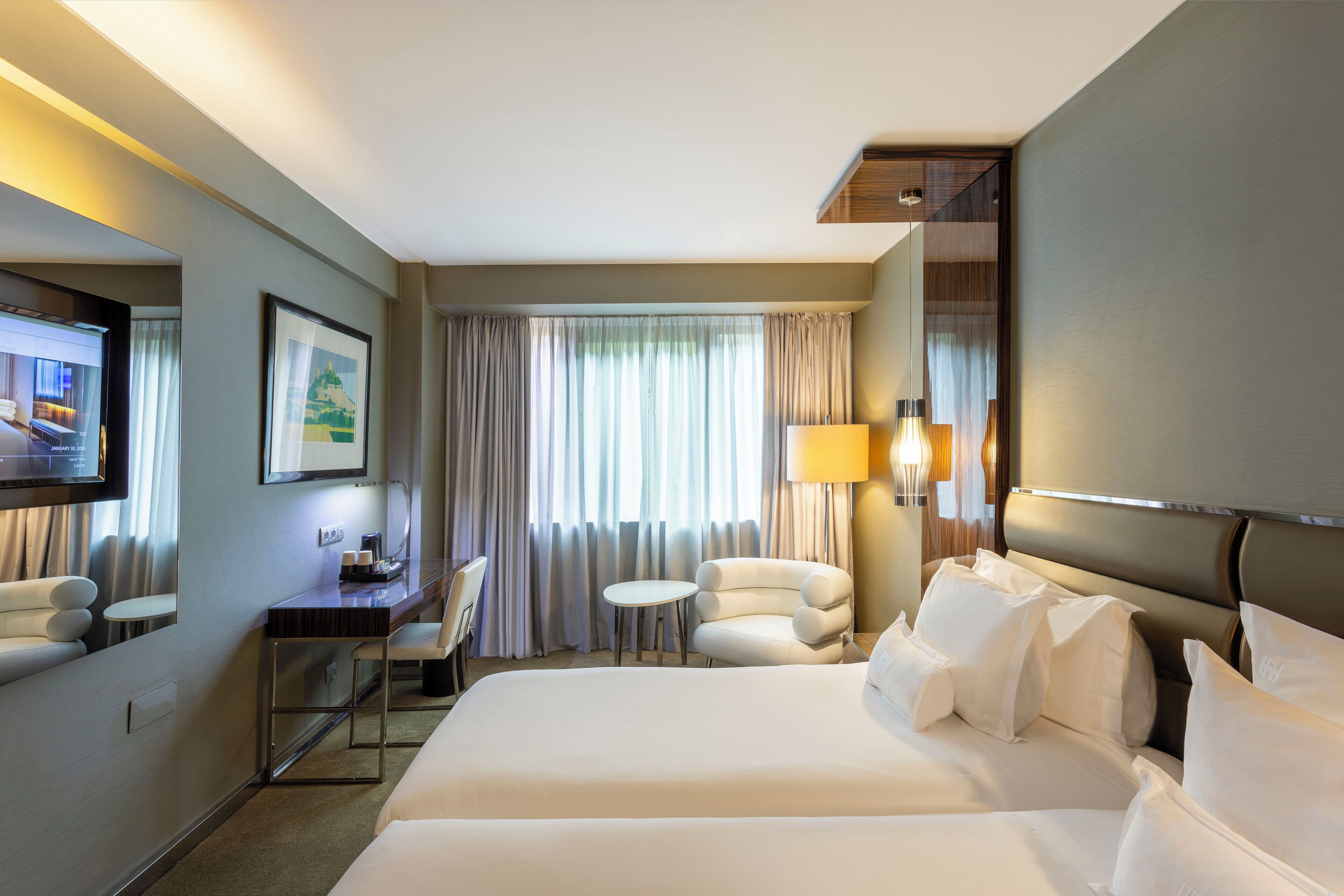 Quarto de hotel com uma cama grande, uma escrivaninha com cadeira, uma mesinha e uma televisão.