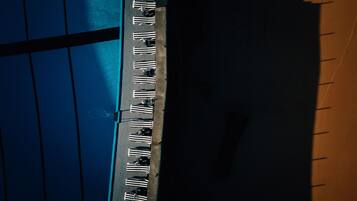 Uma área de piscina com várias espreguiçadeiras alinhadas na borda, um calçadão de concreto e uma piscina azul.