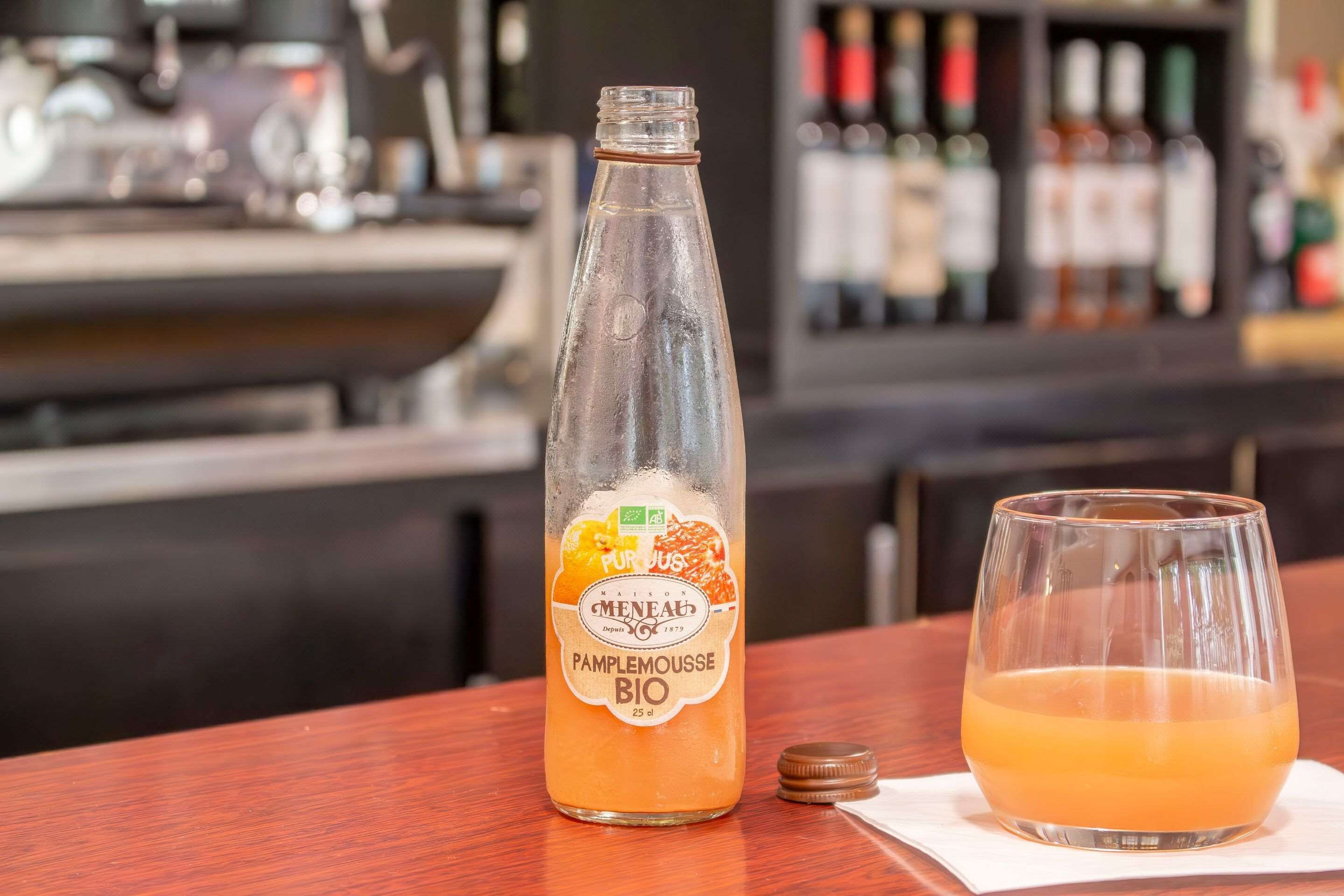 Uma garrafa de suco de pamplemousse bio ao lado de um copo cheio do suco sobre uma mesa de madeira.