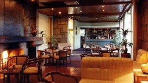Um hall amplo com lareira de pedra, teto de madeira e área de bar com cadeiras e mesas.