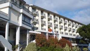 Um hotel com vários andares, varandas, um pátio central com plantas e um céu limpo.