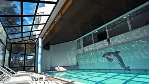 Piscina com mural de golfinho, espreguiçadeiras e teto de vidro.