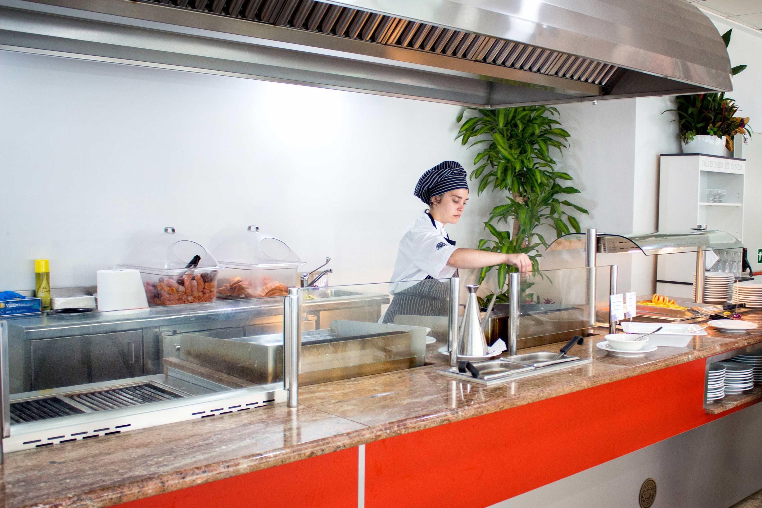 Disposição de buffet com um chefe preparando alimentos, uma pia de aço inoxidável e diversos pratos à mostra.