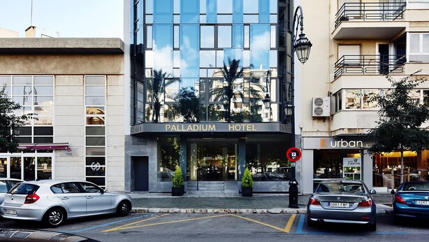 Um hotel moderno com fachada azul, várias varandas e uma entrada visível com a placa "Palladium Hotel".