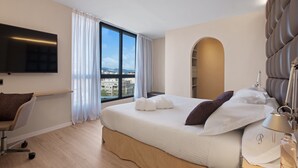 Quarto de hotel moderno com uma cama grande, televisão de tela plana, escrivaninha e vista para a cidade através de grandes janelas.