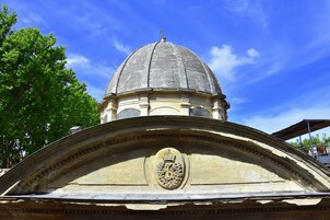 Uma cúpula de pedra com um brasão, rodeada por árvores e um céu límpido.