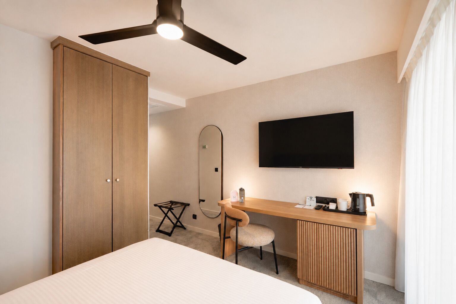 Quarto de hotel com cama, secretária, cadeira, televisão e guarda-roupa.