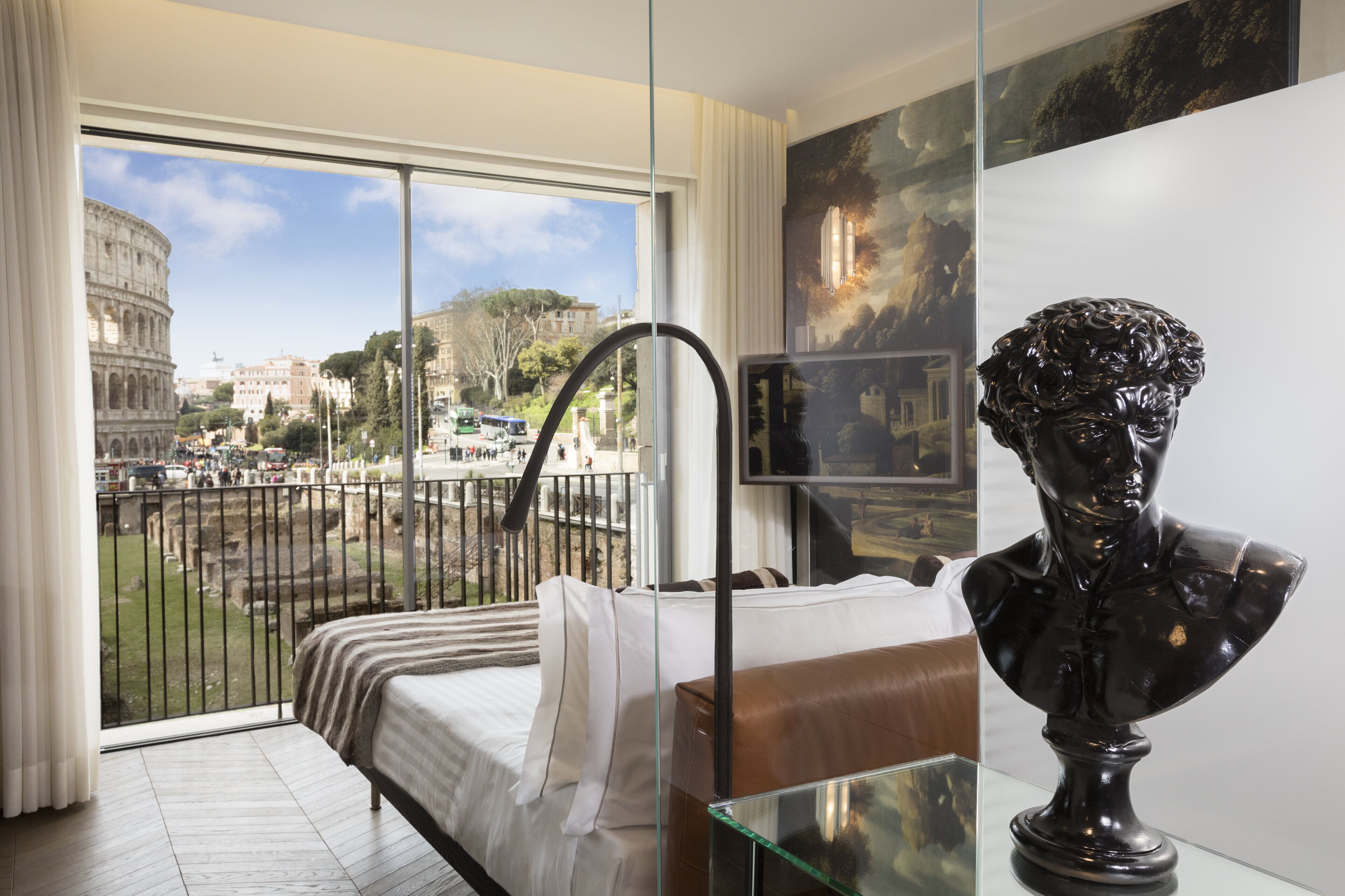 Quarto de hotel com uma cama, uma escultura de busto e vista para o Coliseu.