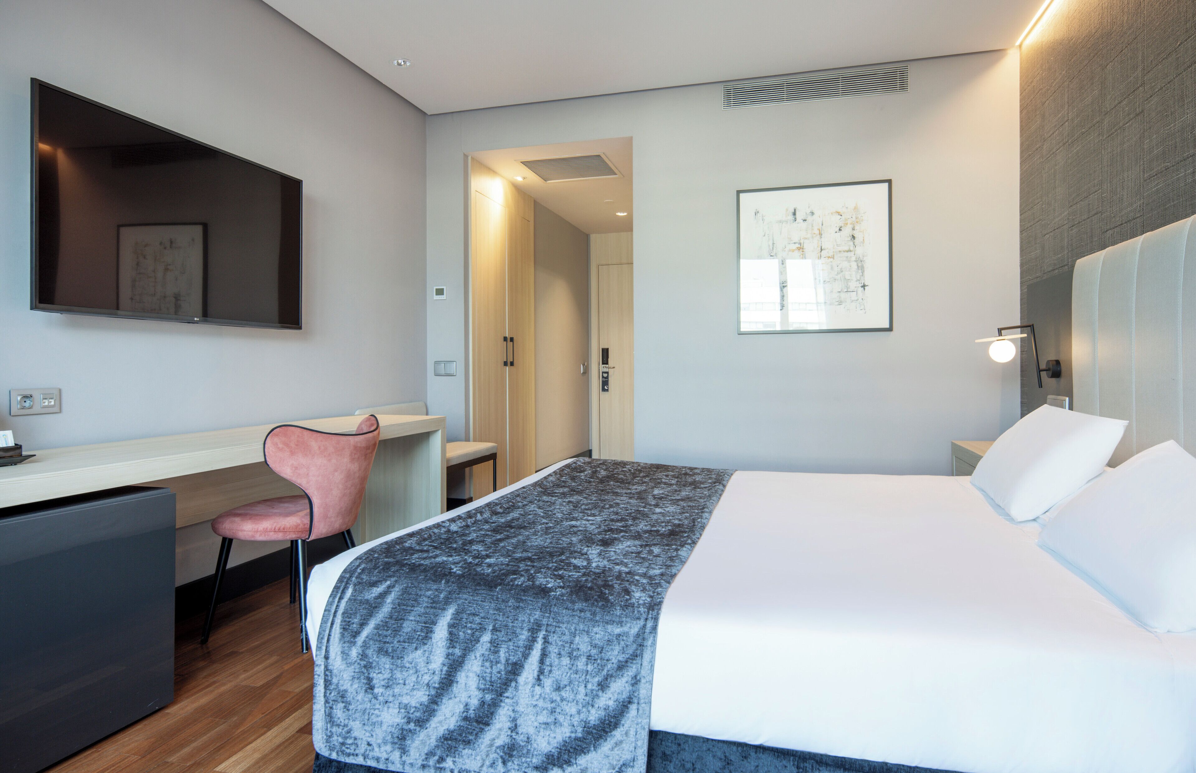 Quarto de hotel moderno com cama, escrivaninha, cadeira e uma janela grande.