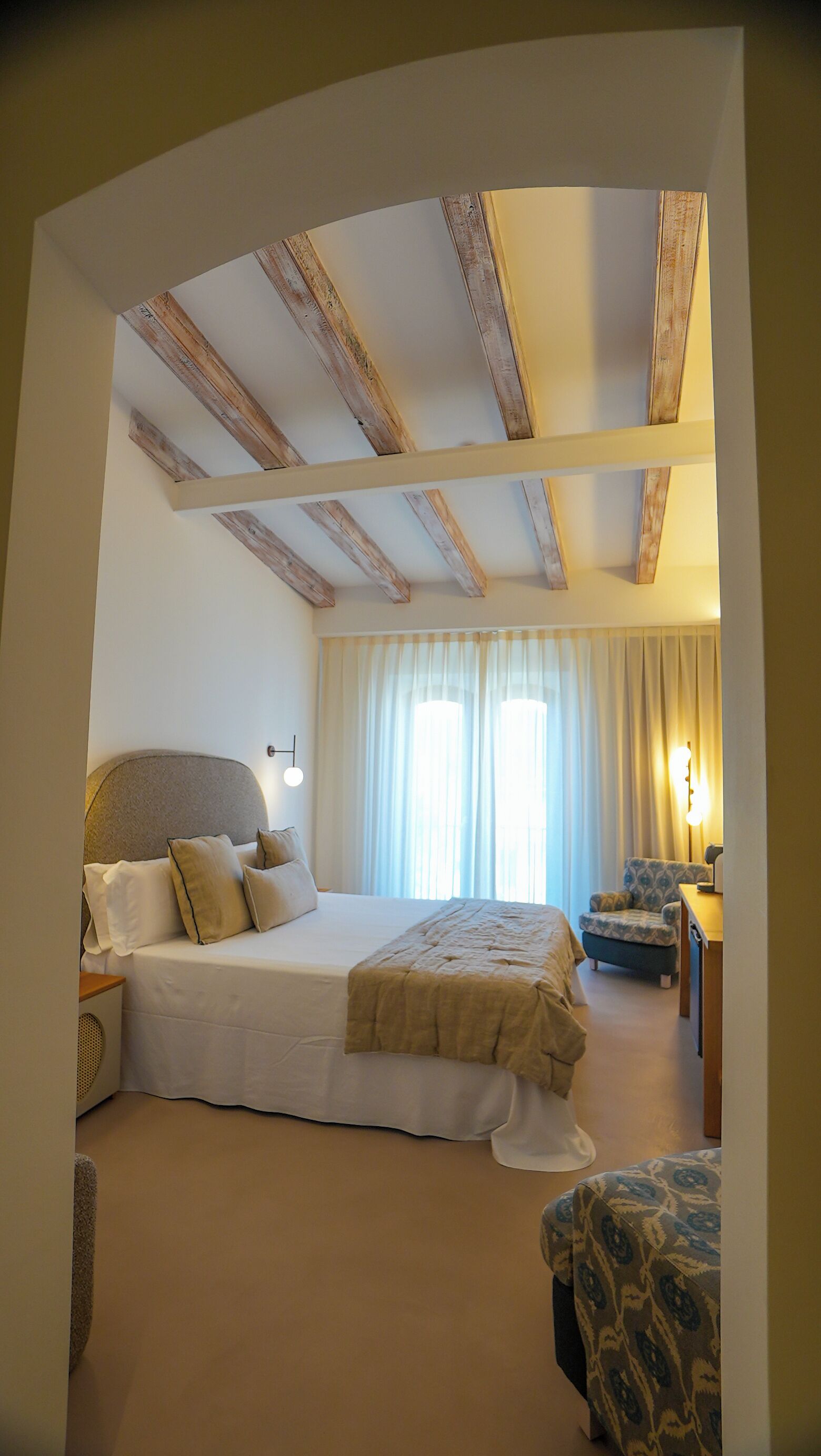 Quarto com uma cama grande, uma cadeira, uma escrivaninha e uma janela com cortinas.