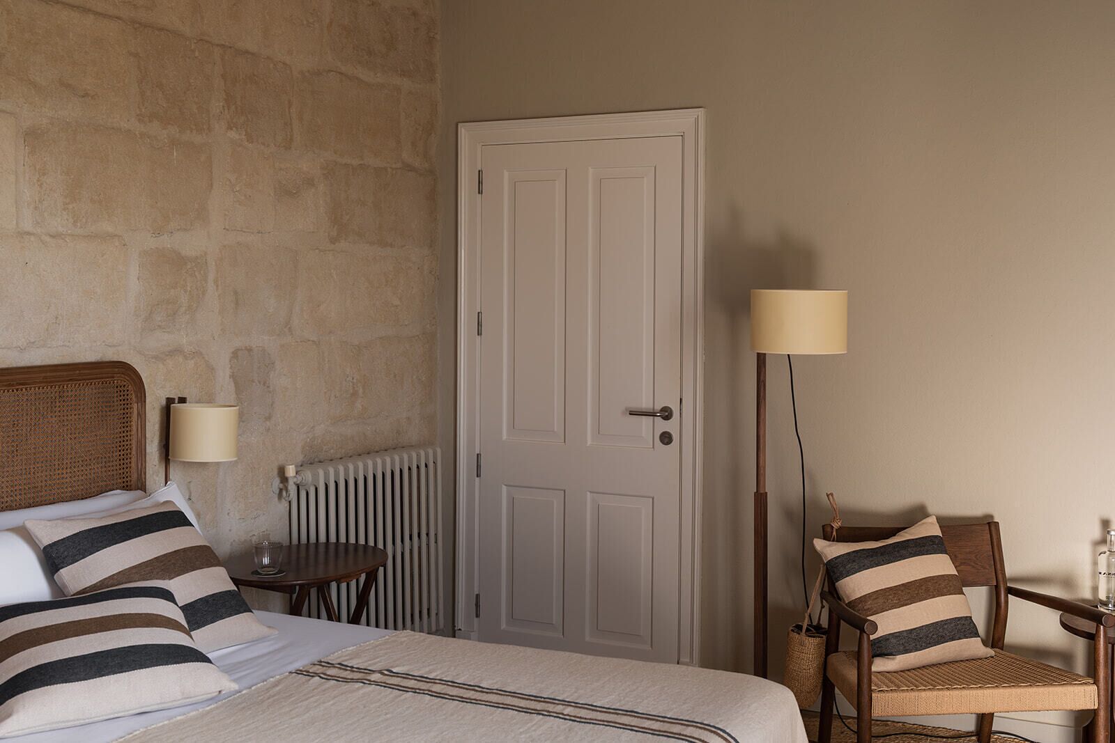 Quarto de hotel com cama, cadeira, abajur e porta.
