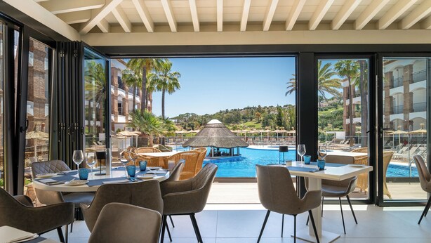 Uma área de jantar moderna com mesas e cadeiras, piscina e vista para um resort.