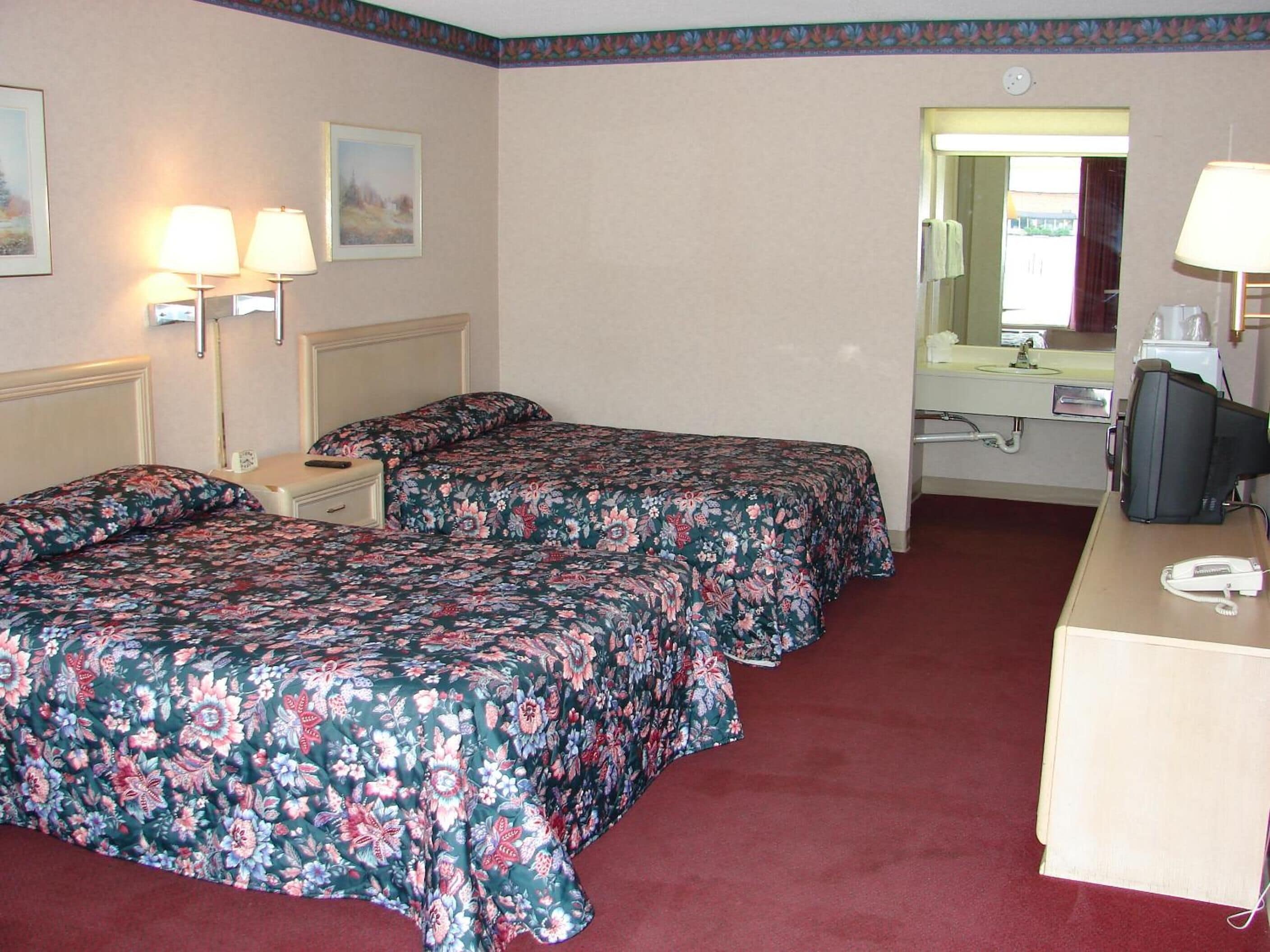 Quarto de hotel com duas camas, uma escrivaninha, um espelho e uma televisão.