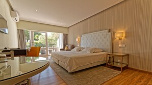 Quarto de hotel moderno com uma cama grande, uma mesa de vidro e vista para o verde lá fora.
