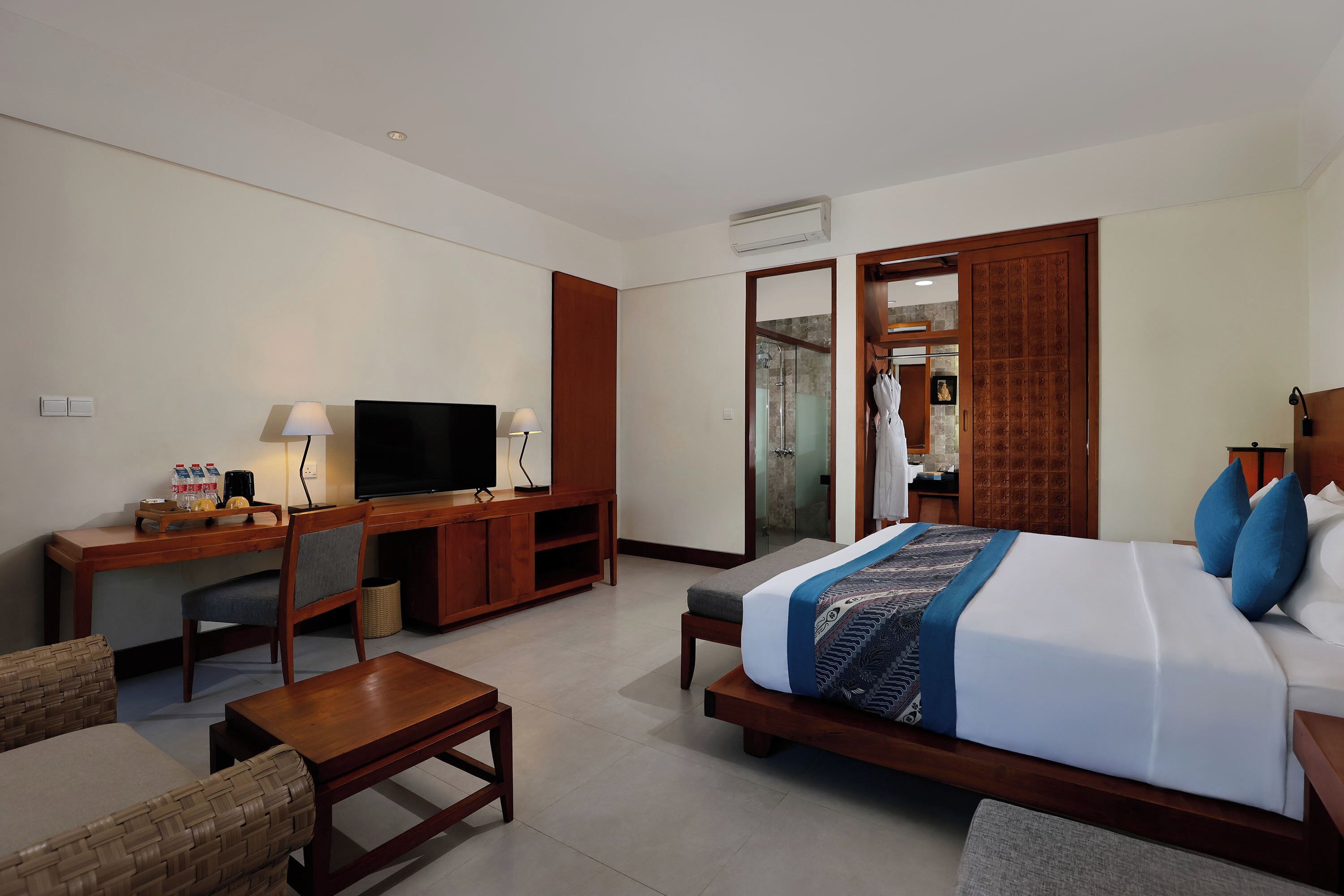 Quarto de hotel com cama, escrivaninha, televisão, cadeira, mesinha de centro e guarda-roupa.
