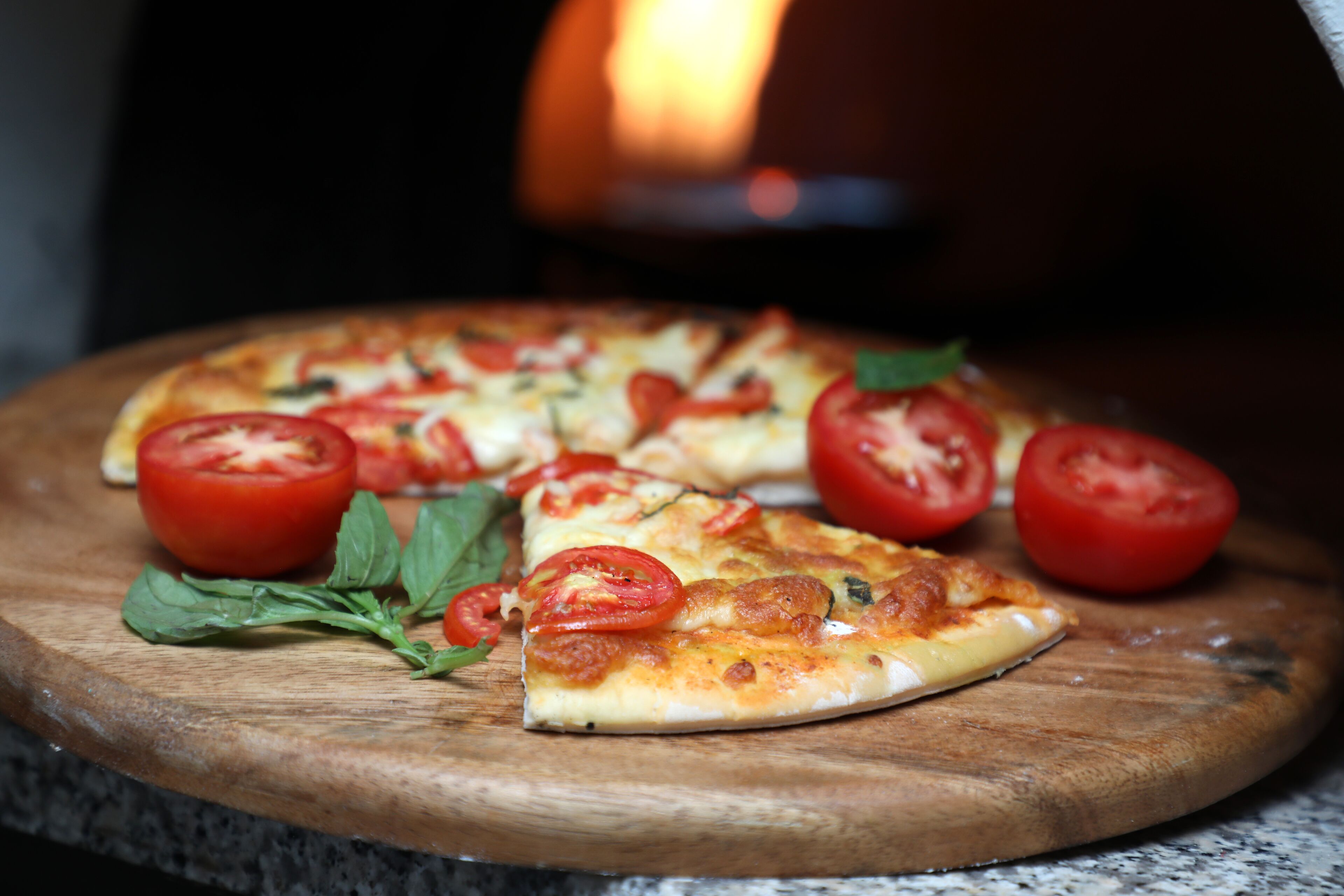 Pizza com rodelas de tomate e manjericão sobre uma tábua de madeira.