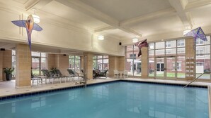 Piscina interna com espreguiçadeiras e mesas, janelas amplas e decorações penduradas.