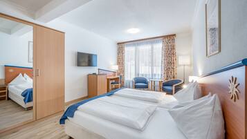 Quarto de hotel com duas camas, uma mesa, uma cadeira, uma televisão e uma janela com cortinas.