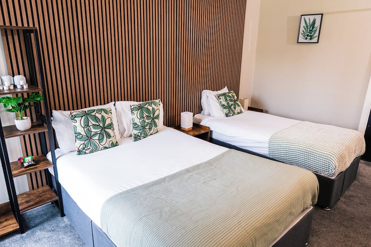 Quarto de hotel com duas camas, parede de ripas de madeira, prateleira com objetos e um quadro na parede.