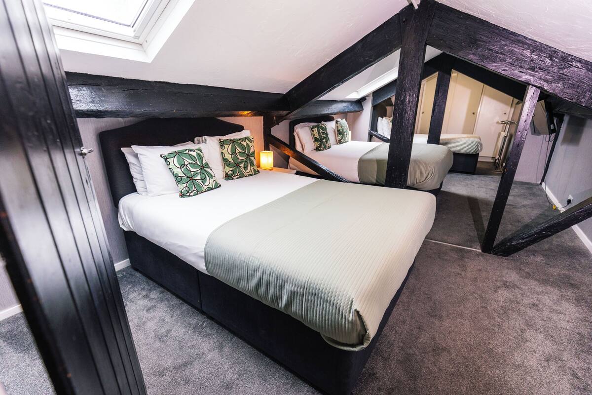 Quarto com cama estilo loft, claraboia e espelho refletindo o ambiente.