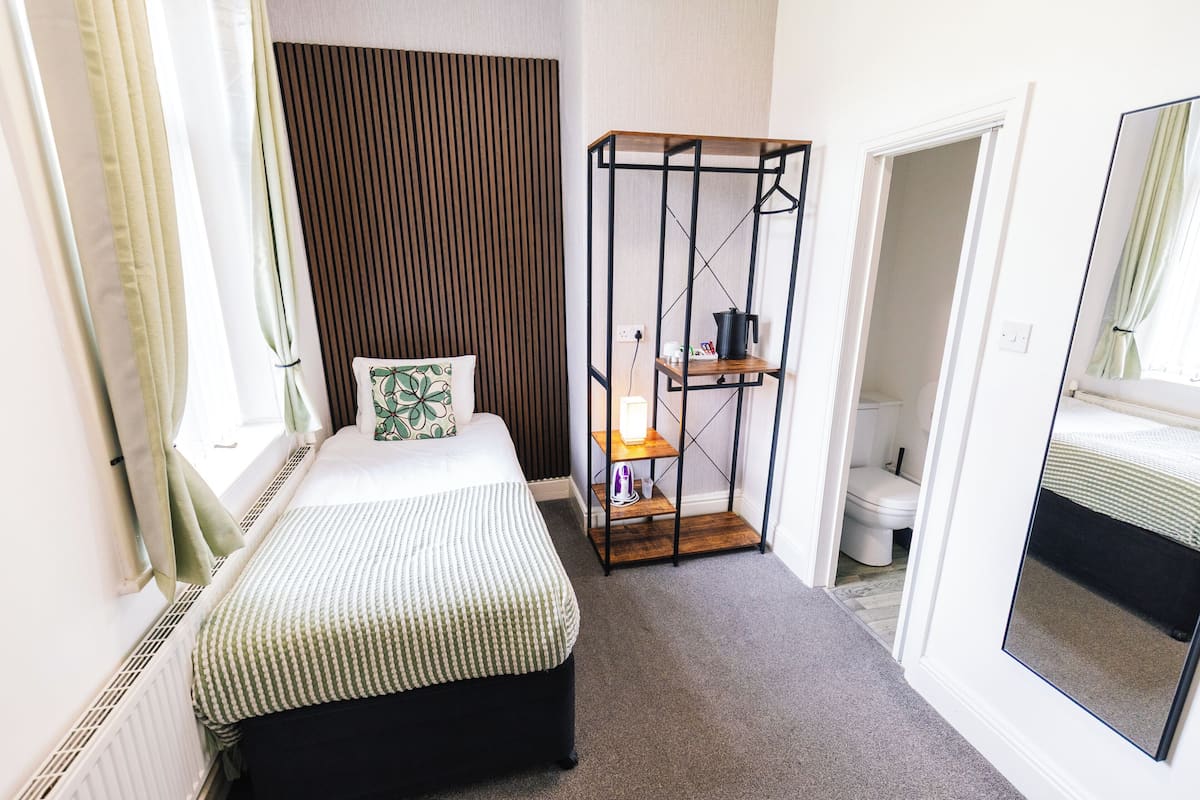 Quarto de hotel com cama, mesa de cabeceira, guarda-roupa e casa de banho visível através de uma porta aberta.