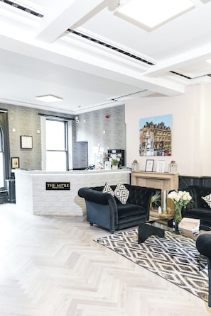 Um saguão de hotel com uma mesa de recepção, lareira, uma janela grande e um quadro na parede.