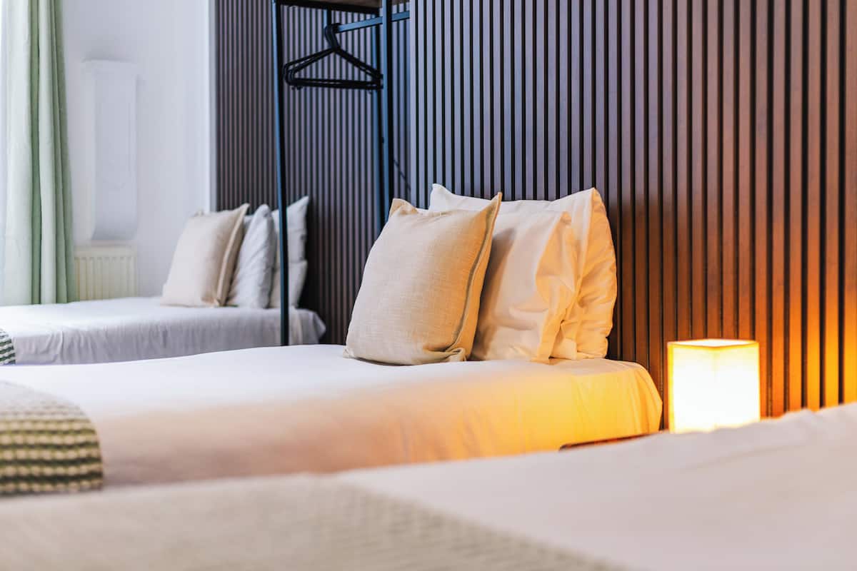 Quarto de hotel com duas camas, uma luminária pendente e um radiador.