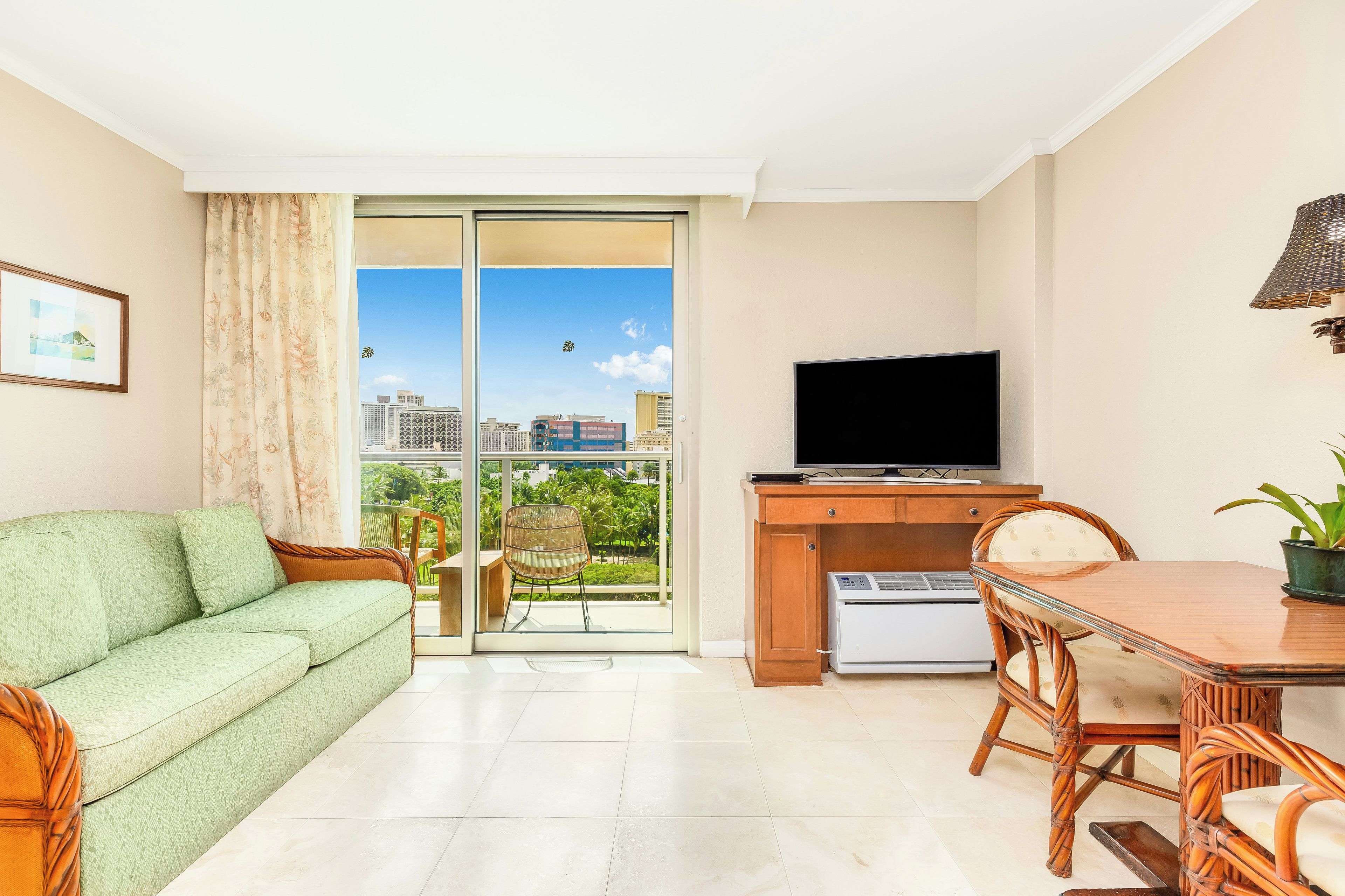 Uma sala de estar moderna com um sofá verde, uma mesa de jantar com cadeiras, uma televisão de tela plana e vista para a cidade através de uma porta de vidro.