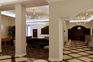 Um lobby de hotel com piso xadrez, um sofá, uma mesa de centro e um lustre.
